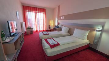 Quarto de hotel com duas camas, uma escrivaninha, televisão e janela com cortinas.