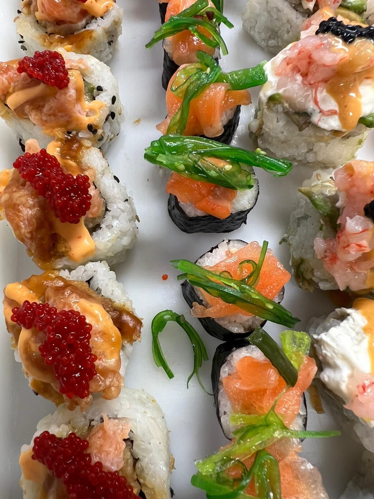 Diversos tipos de sushi com coberturas como salmão, caviar e cebolinha.