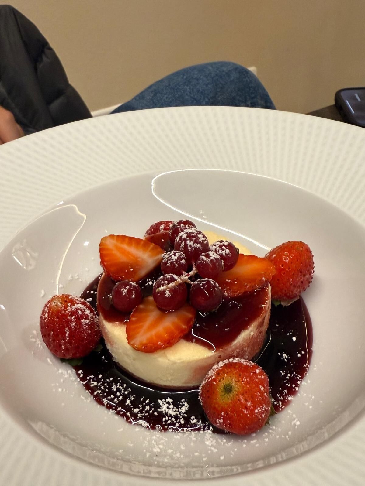 Um prato de sobremesa com uma sobremesa cremosa, morangos e cerejas em um prato branco.