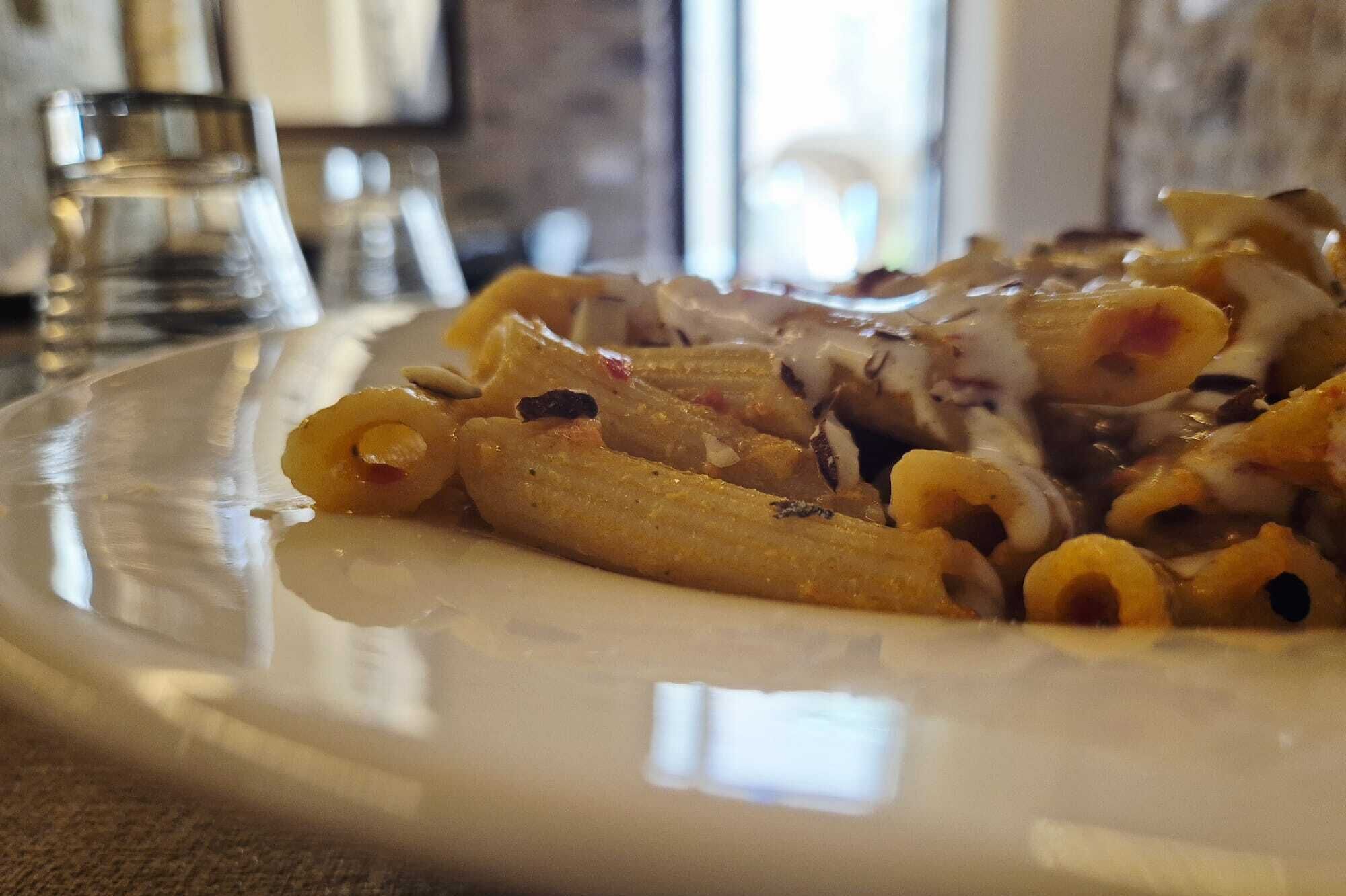 Um prato de massa com molho cremoso, decorado com ervas e nozes, sobre um prato branco.
