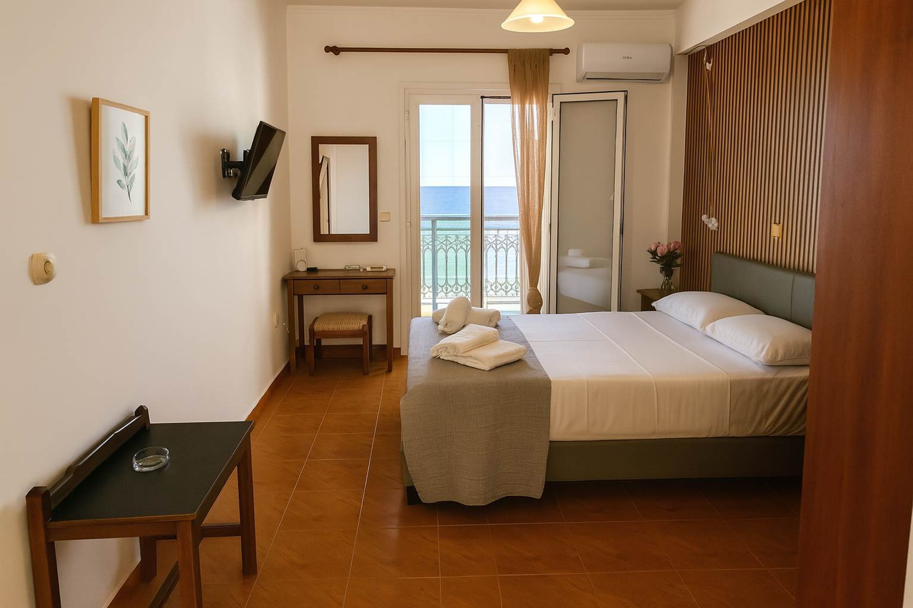 Quarto de hotel com uma cama, escrivaninha, cadeira, televisão, janela e porta.