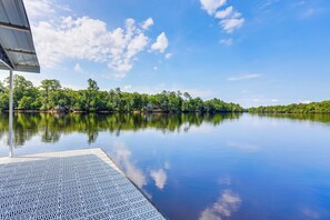 Um lago tranquilo com um cais se estendendo na água, rodeado por árvores densas e um céu claro.