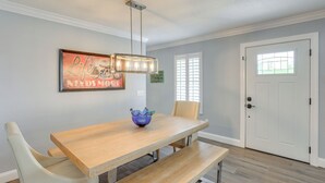 Uma área de refeições com mesa de madeira, bancos e cadeiras. Há uma tigela decorativa sobre a mesa, uma luminária pendente e um quadro na parede.