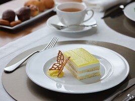 Prato com fatia de bolo em camadas sobre prato branco, acompanhado de uma xícara de café e um garfo sobre a mesa.