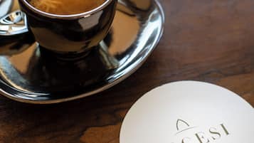 Uma chávena de café sobre um pires refletor, ao lado de um cartão de visita com o nome 'ASCESI' e quatro estrelas.