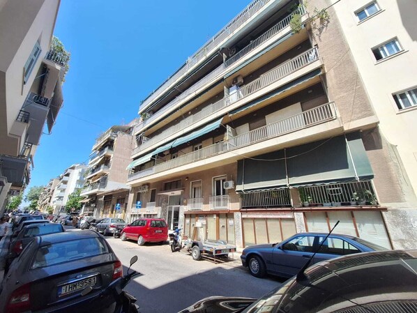 Um edifício residencial com várias andares, varandas, carros estacionados e um céu azul claro.