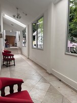 Um corredor com amplas janelas, escadas e cadeiras vermelhas.