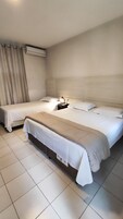 Quarto de hotel com duas camas, uma mesa de cabeceira com abajur e um aparelho de ar condicionado na parede.