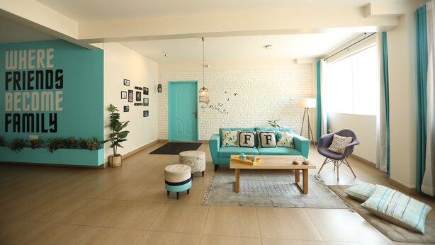 Uma sala de estar com uma parede de destaque verde-azulado, uma parede de tijolos brancos, uma porta azul, um sofá com almofadas estampadas com a palavra 'FAMILY', uma mesa de centro e um abajur.