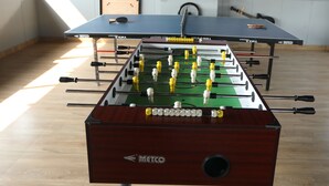 Uma mesa de futebol de mesa em um quarto com uma janela grande, uma guitarra e uma tela de TV.
