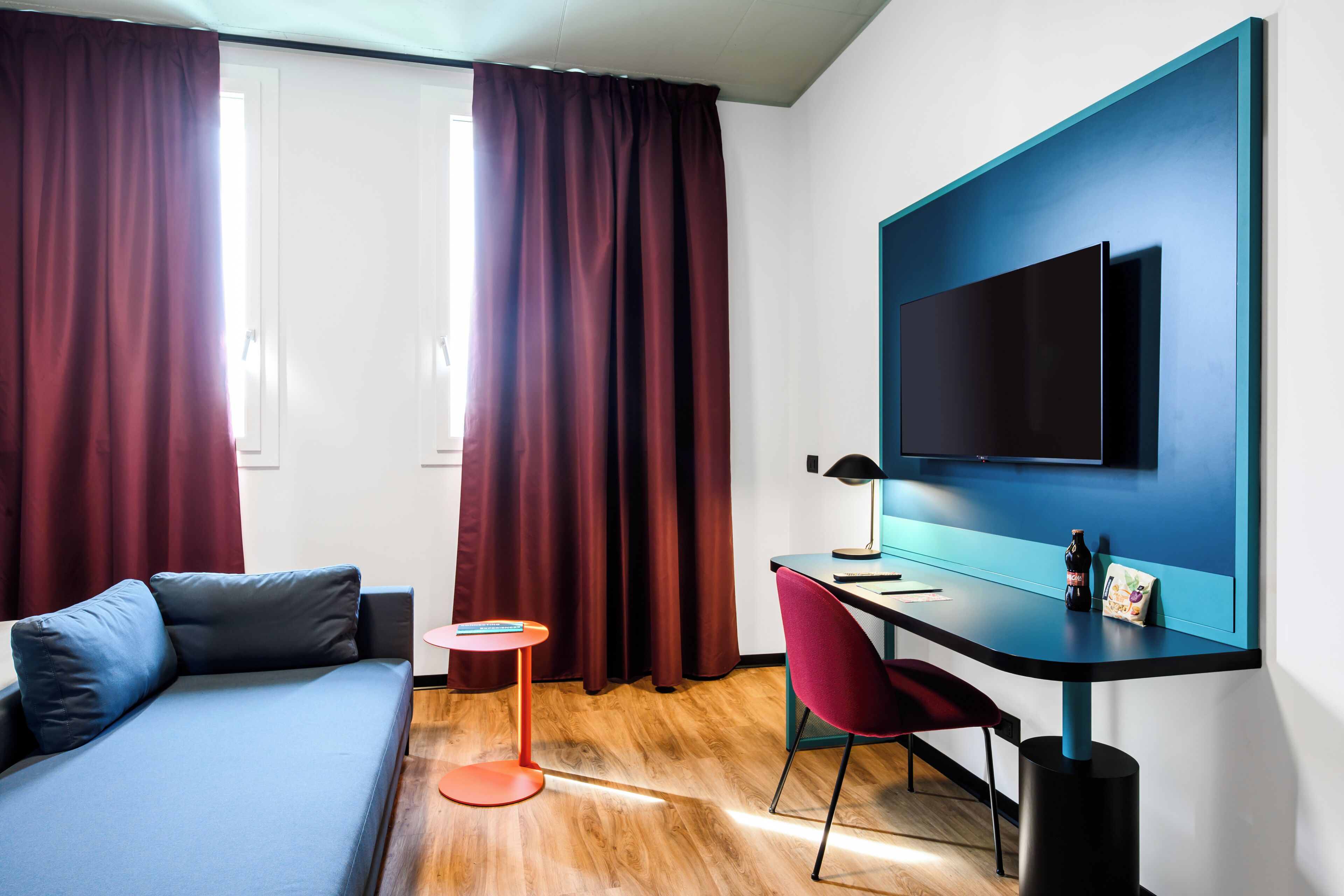 Quarto de hotel moderno com uma cama, uma escrivaninha, uma cadeira e uma televisão na parede.