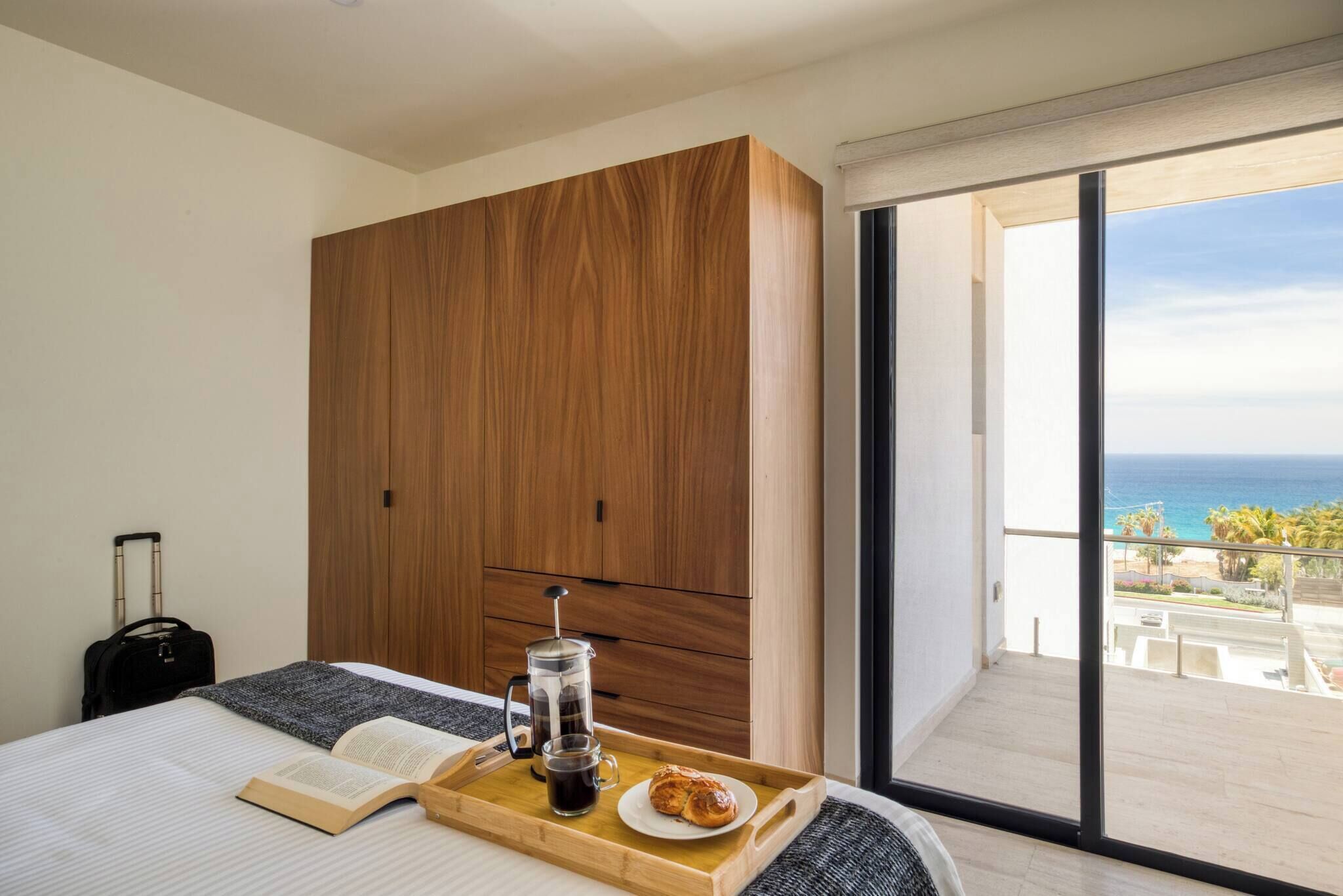 Quarto com um guarda-roupa de madeira grande, uma cama com bandeja de café da manhã e vista para o oceano através de uma varanda.
