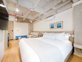 Quarto de hotel moderno com uma cama grande, uma televisão de tela plana, uma mesinha e um banquinho azul.