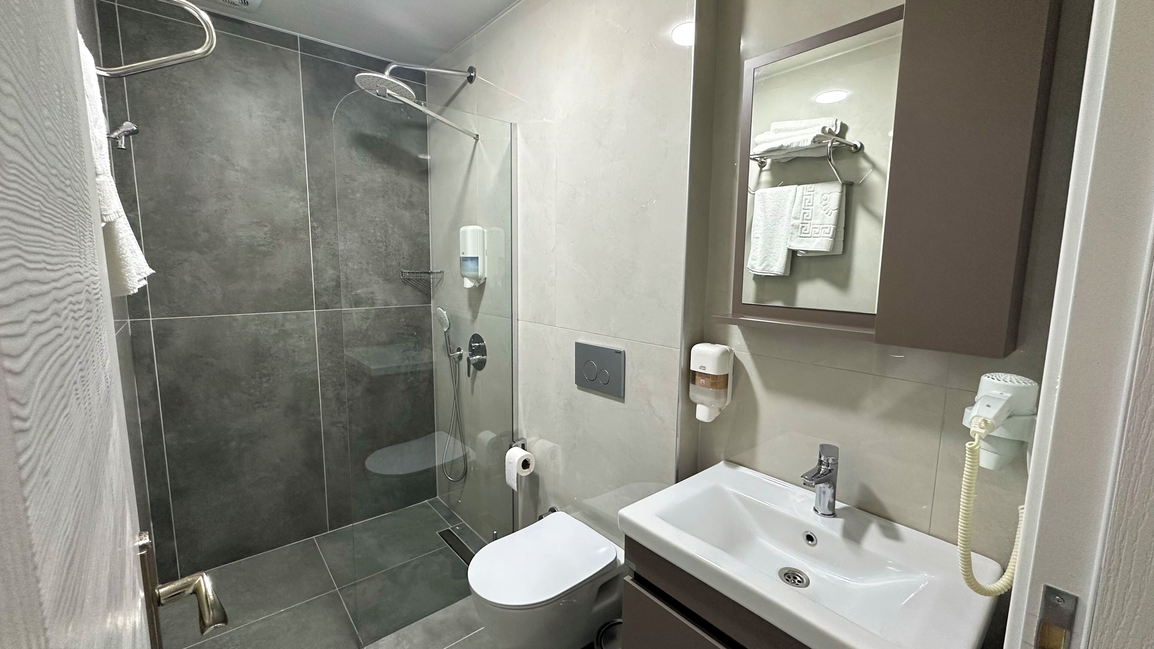 Um banheiro moderno com box de vidro, vaso sanitário, pia com espelho e porta-toalhas.