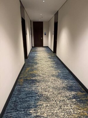 Um corredor com carpete texturizado, paredes e uma porta no final.