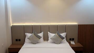 Quarto de hotel com cama grande, iluminação na cabeceira, duas mesas de cabeceira e piso coberto por carpete.