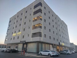 Um hotel de vários andares com design moderno, apresentando varandas em cada pavimento, um spa no térreo e um estacionamento com vários carros.