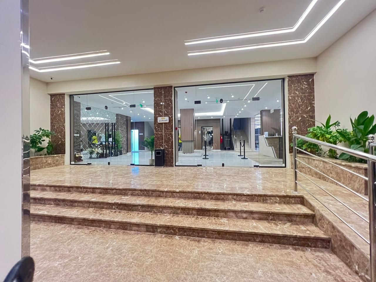 Um hall de hotel com piso de mármore, escada e entrada de vidro.