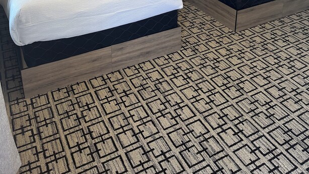 Quarto de hotel com duas camas, um tapete estampado e uma luminária no teto.