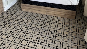 Uma cama bem arrumada com cabeceira de madeira, tapete estampado e duas luminárias fixadas na parede.
