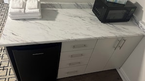 Cozinha com bancada de mármore, micro-ondas preto e uma pilha de toalhas brancas.