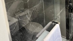 Casa de banho moderna com cabine de chuveiro em vidro e azulejos de mármore.