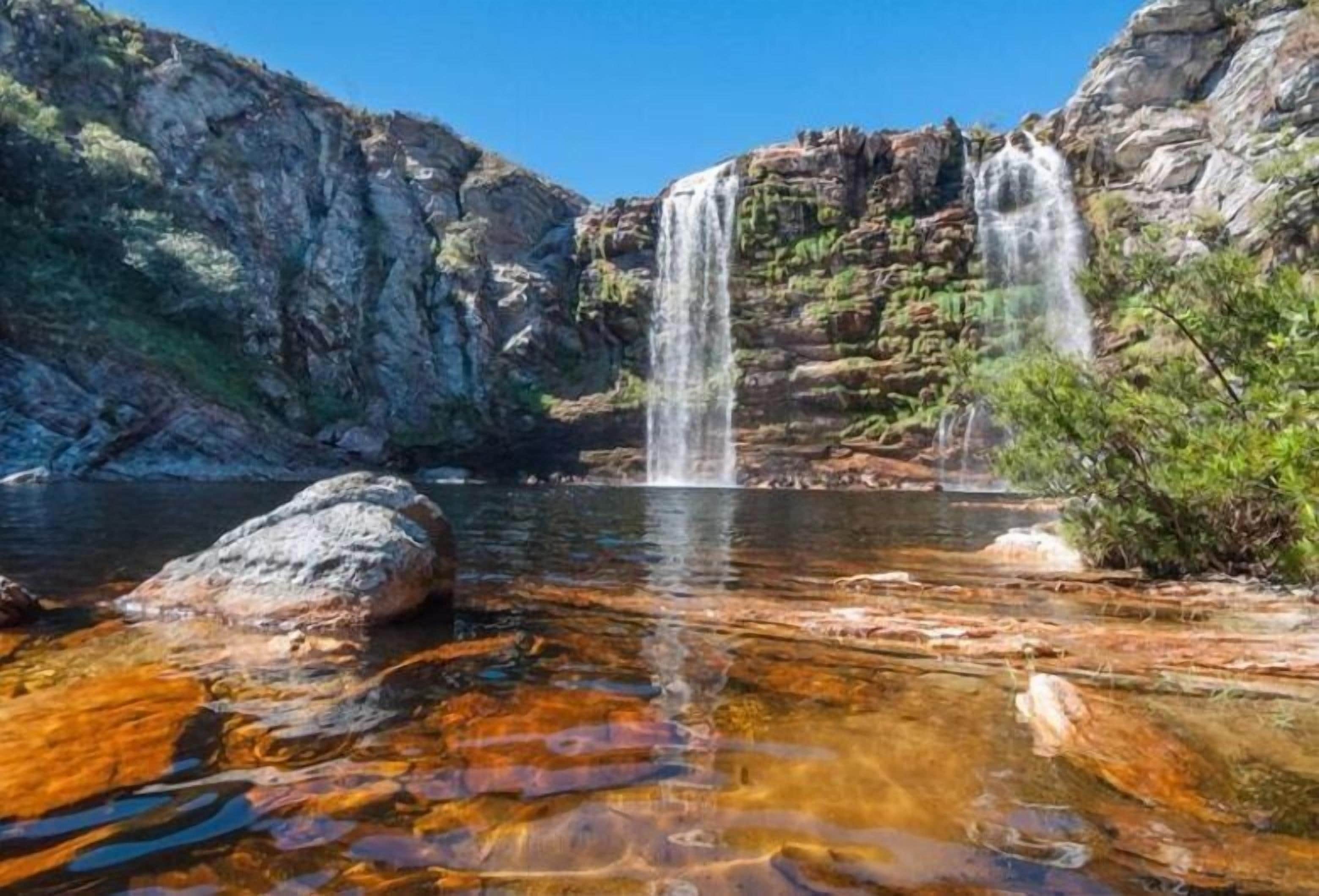 Paisagem natural com uma cascata, água cristalina e terreno rochoso.