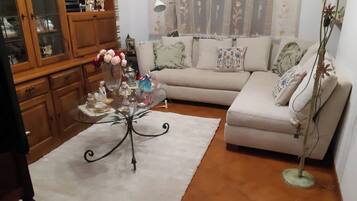Sala de estar com mesa de centro de vidro, sofá bege, tapete branco e luminária de chão alta.