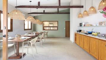 Uma sala de jantar espaçosa com uma longa mesa de madeira e cadeiras, uma área de cozinha com armários de madeira e bancada, e luminárias de bambu pendentes.