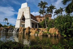 Um resort com um edifício branco imponente, uma cachoeira e palmeiras.