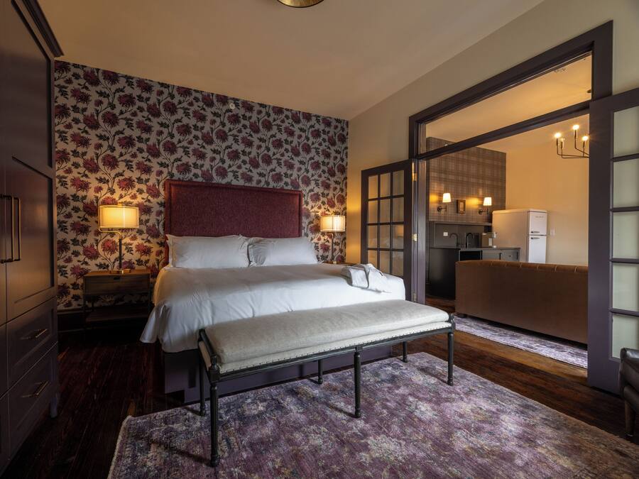 Quarto com uma cama grande, um banco, uma cômoda e uma mesa de cabeceira.