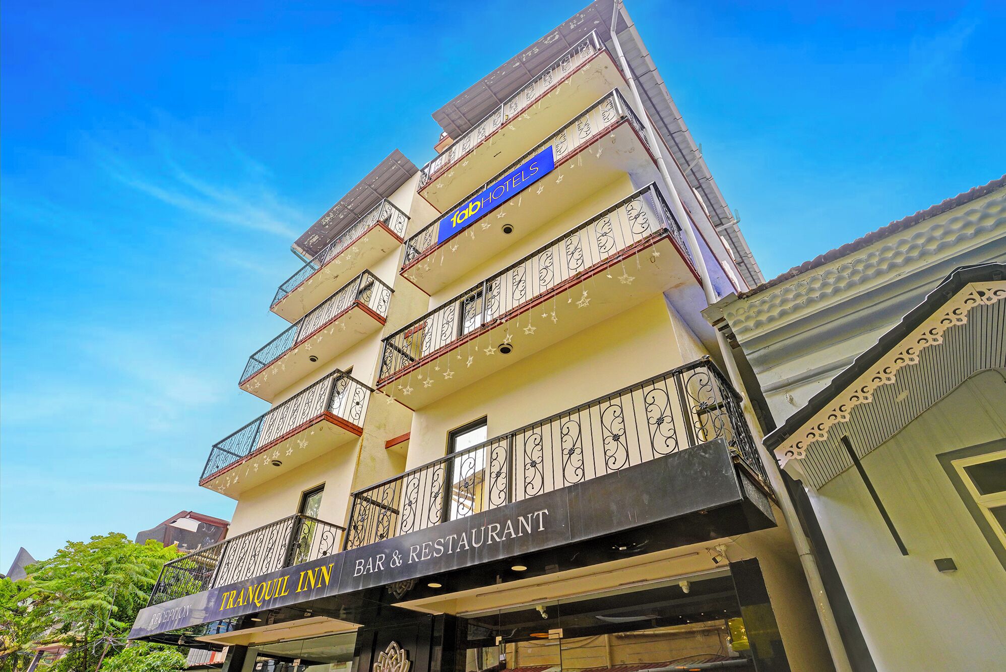 Um edifício com vários andares e varandas, um bar e restaurante no andar térreo, e uma placa com o nome 'Tranquil Inn'.