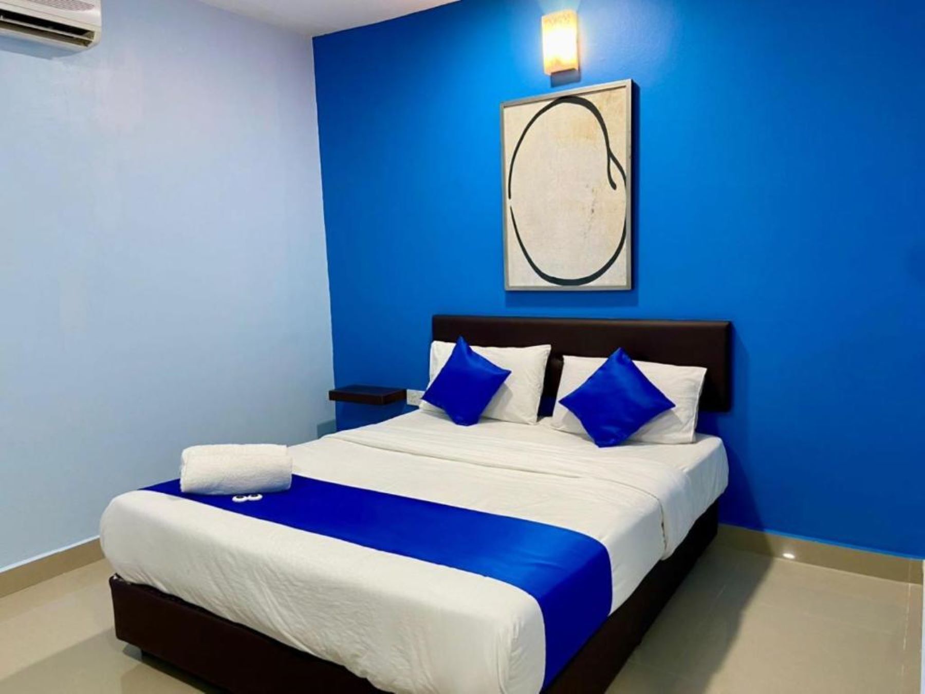 Quarto de hotel com cama, paredes azuis, cabeceira branca e um quadro na parede.