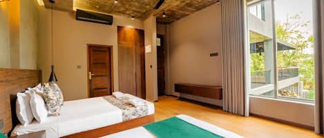 Quarto de hotel moderno com duas camas, um ventilador de teto, uma janela ampla com vista para o verde e um banco embutido.