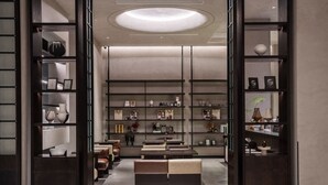 Um interior moderno com uma área de estar central, prateleiras com diversos objetos e uma luminária no teto.