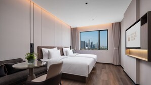 Quarto de hotel moderno com vista para a cidade, um sofá, uma mesa redonda e uma cama com roupa de cama branca.