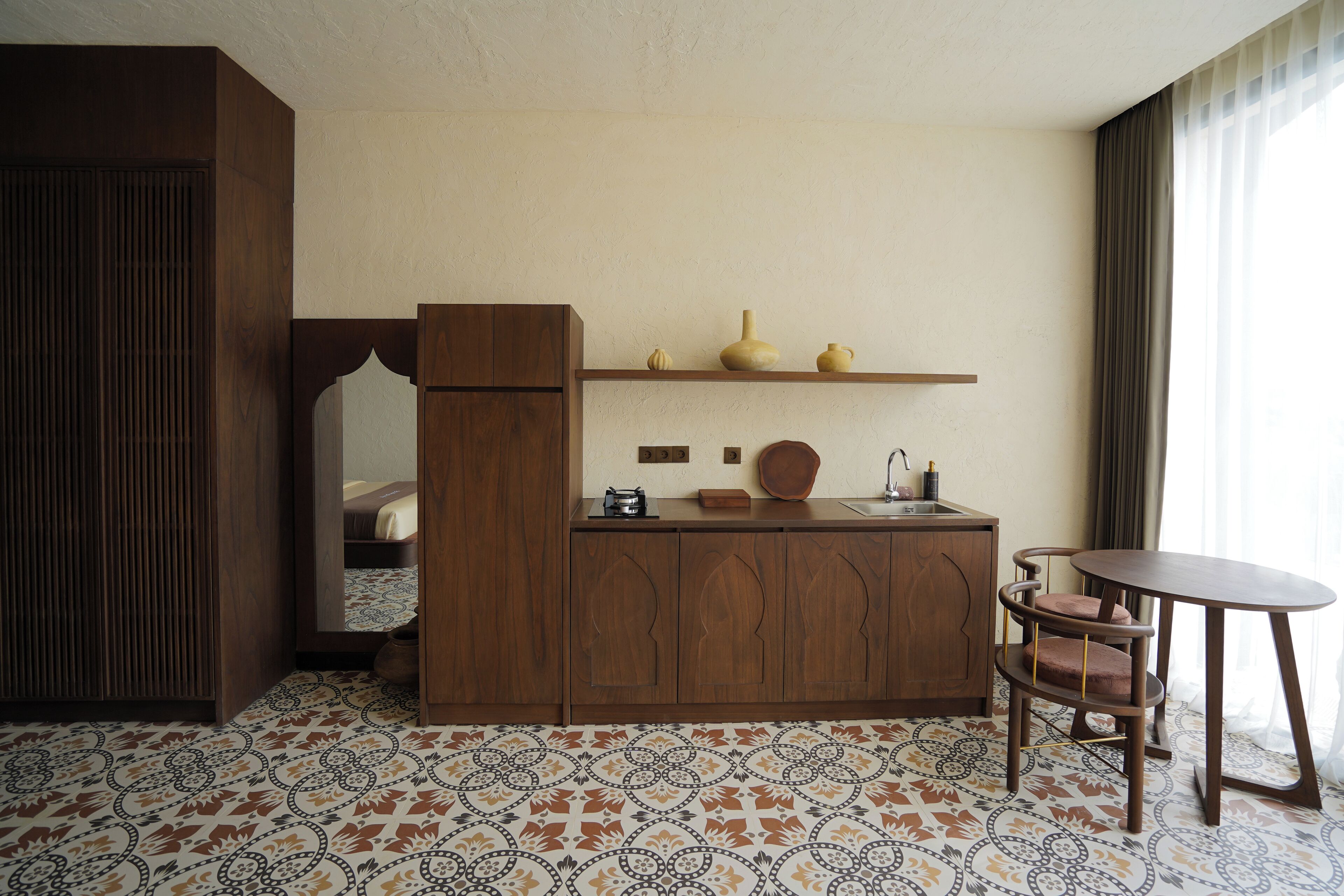 Quarto de hotel pequeno com um armário de madeira, pia, espelho e uma mesa redonda com cadeiras.