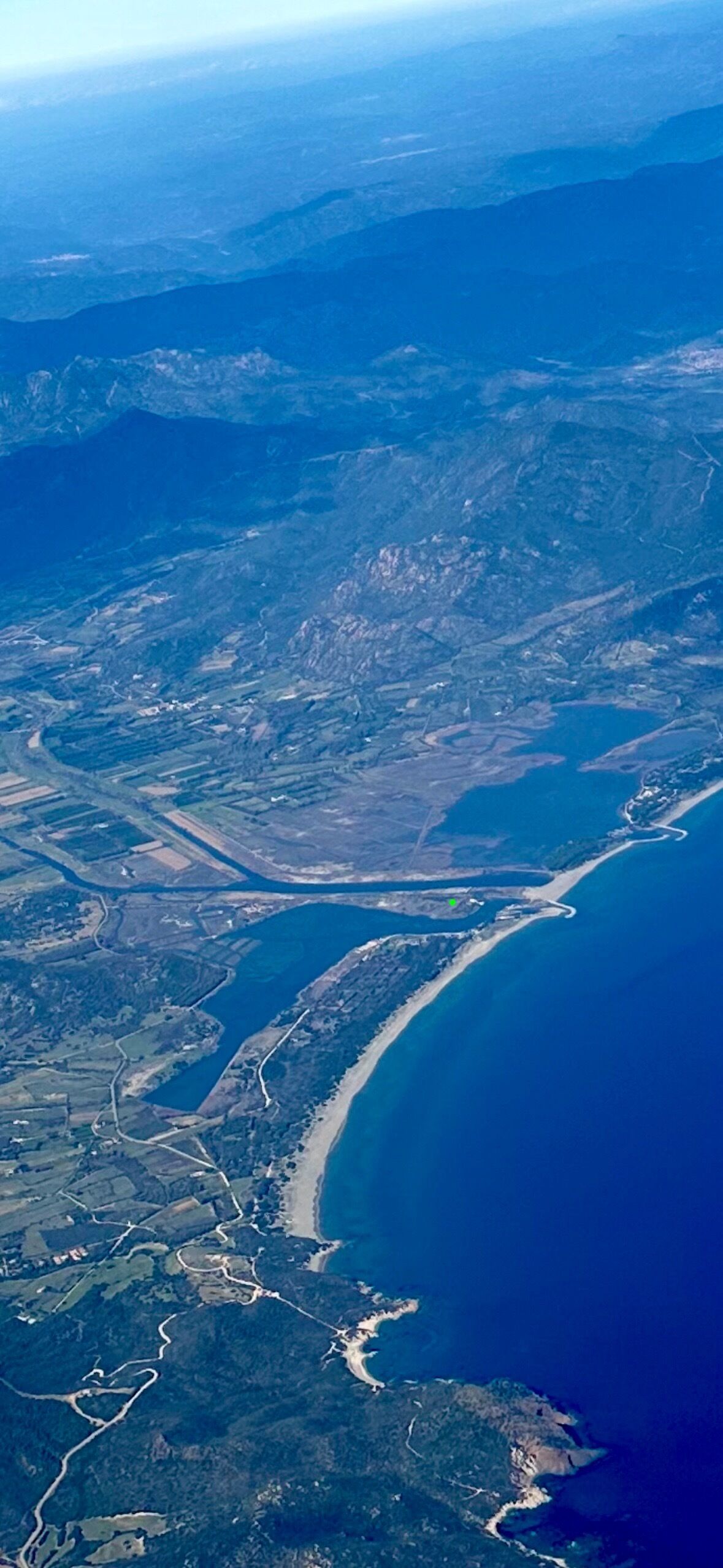 Vista aérea de uma área costeira com uma estrada sinuosa, vegetação densa e uma grande extensão de água.