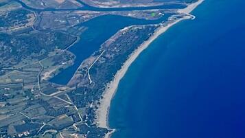 Vista aérea de uma área costeira com uma estrada sinuosa, vegetação densa e uma grande extensão de água.