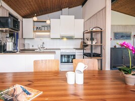 Uma cozinha moderna com armários brancos, bancada de madeira e uma área de refeições com mesa e cadeiras de madeira.