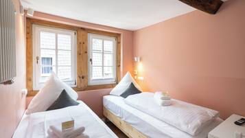 Quarto com duas camas, cabeceira de madeira, mesa de cabeceira e janela com portadas.