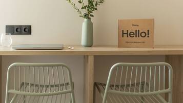 Uma mesa com um laptop, um vaso com folhas verdes, um aviso com a palavra 'Hello!' e duas cadeiras brancas.