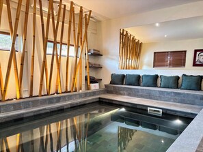 Uma área interna de piscina moderna, com decoração em bambu, assentos de pedra e piscina transparente.