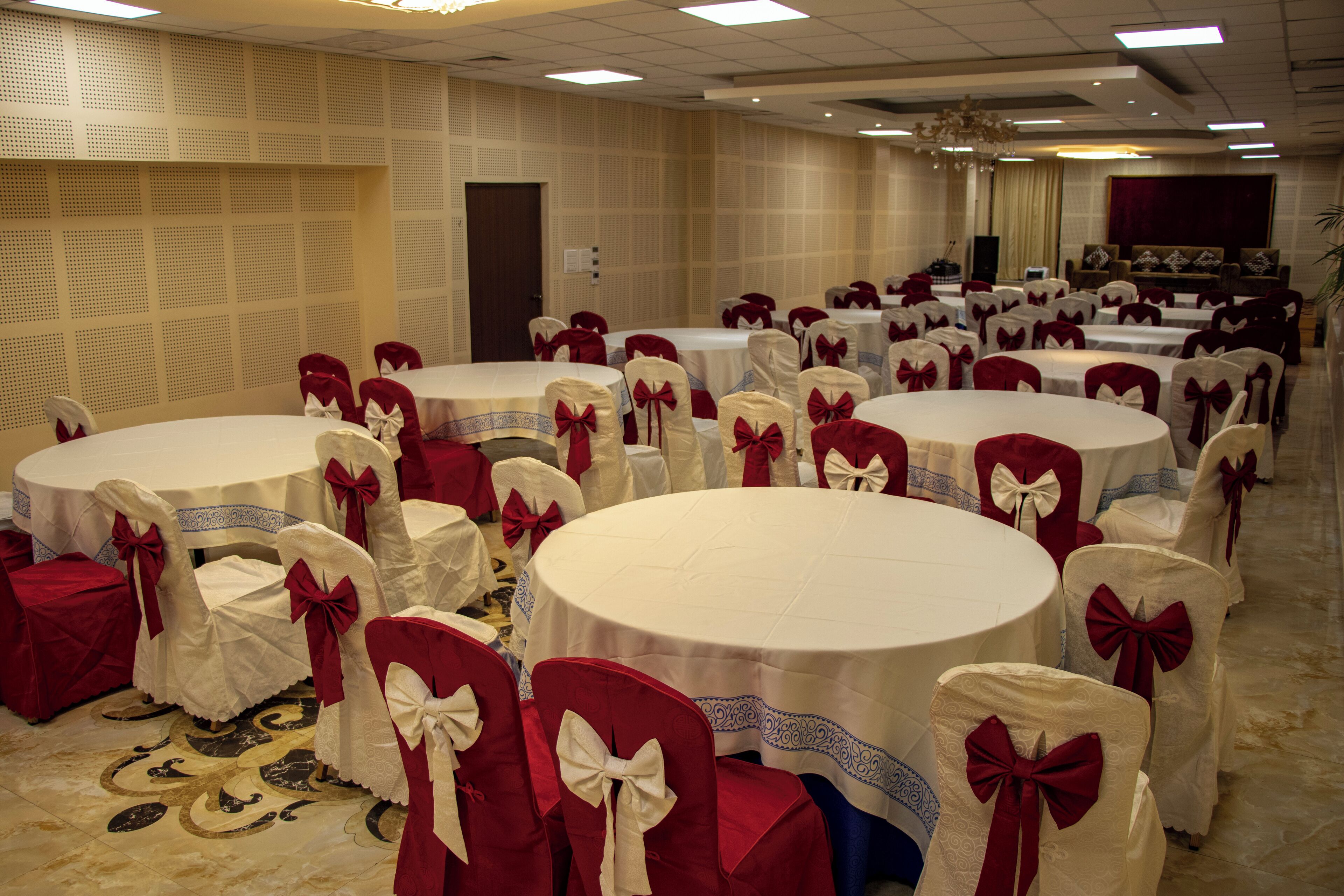 Uma sala de banquetes com mesas redondas cobertas por toalhas brancas e cadeiras vermelhas com laços brancos.
