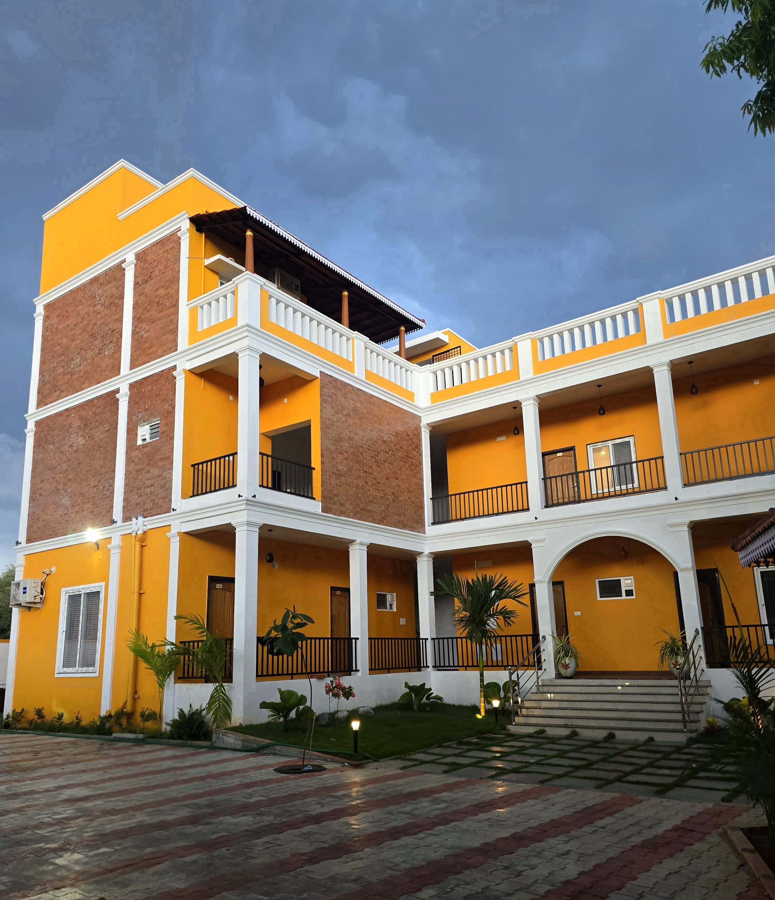 Um edifício de vários andares com paredes externas amarelas e brancas, várias varandas e um pátio central com plantas em vasos.