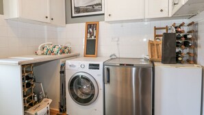 Uma cozinha compacta com máquina de lavar, geladeira de aço inoxidável, suporte para vinhos e um quadro na parede.