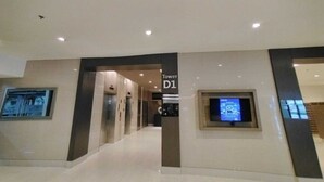 Um corredor moderno de hotel com elevadores, uma tela digital de informações e uma placa indicando 'Tower D1'.