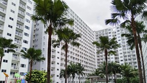 Um hotel moderno com vários andares, área de estar externa junto a uma piscina e palmeiras.