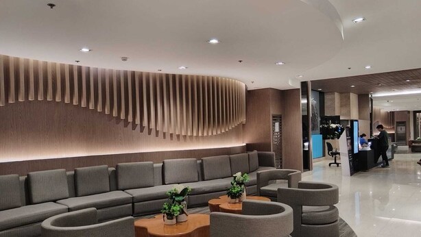 Um lobby moderno com um sofá curvo, mesas de centro redondas e um balcão de recepção.