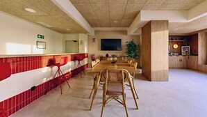 Uma sala de jantar de hotel com uma longa mesa de madeira, cadeiras vermelhas, uma televisão e uma planta.